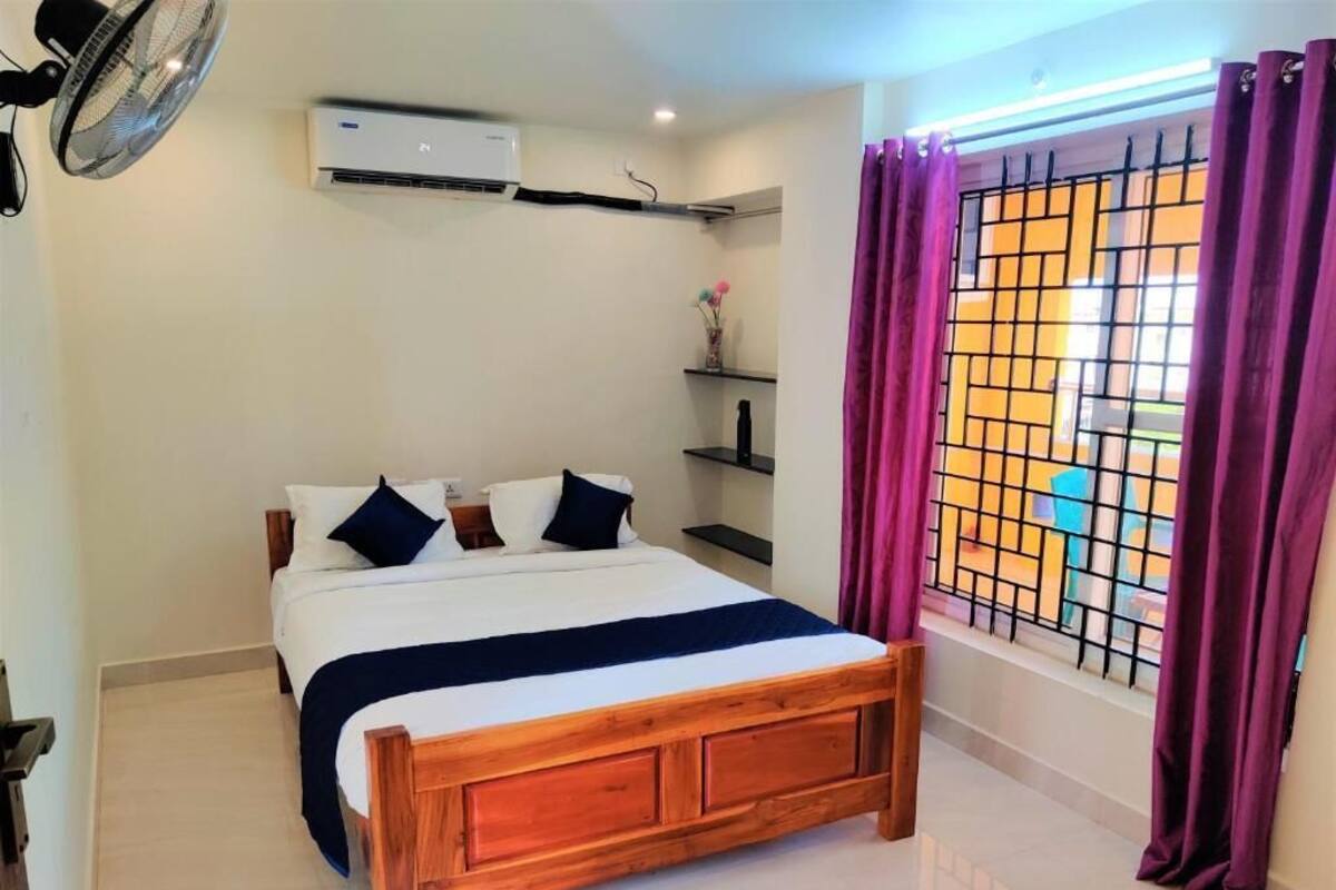 Quarto com cama de madeira, ar condicionado e janela com cortinas roxas.