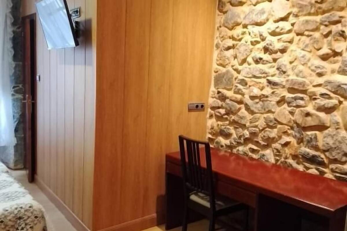 Quarto com parede de painel de madeira, parede de destaque em pedra, escrivaninha com cadeira e televisão fixada na parede.