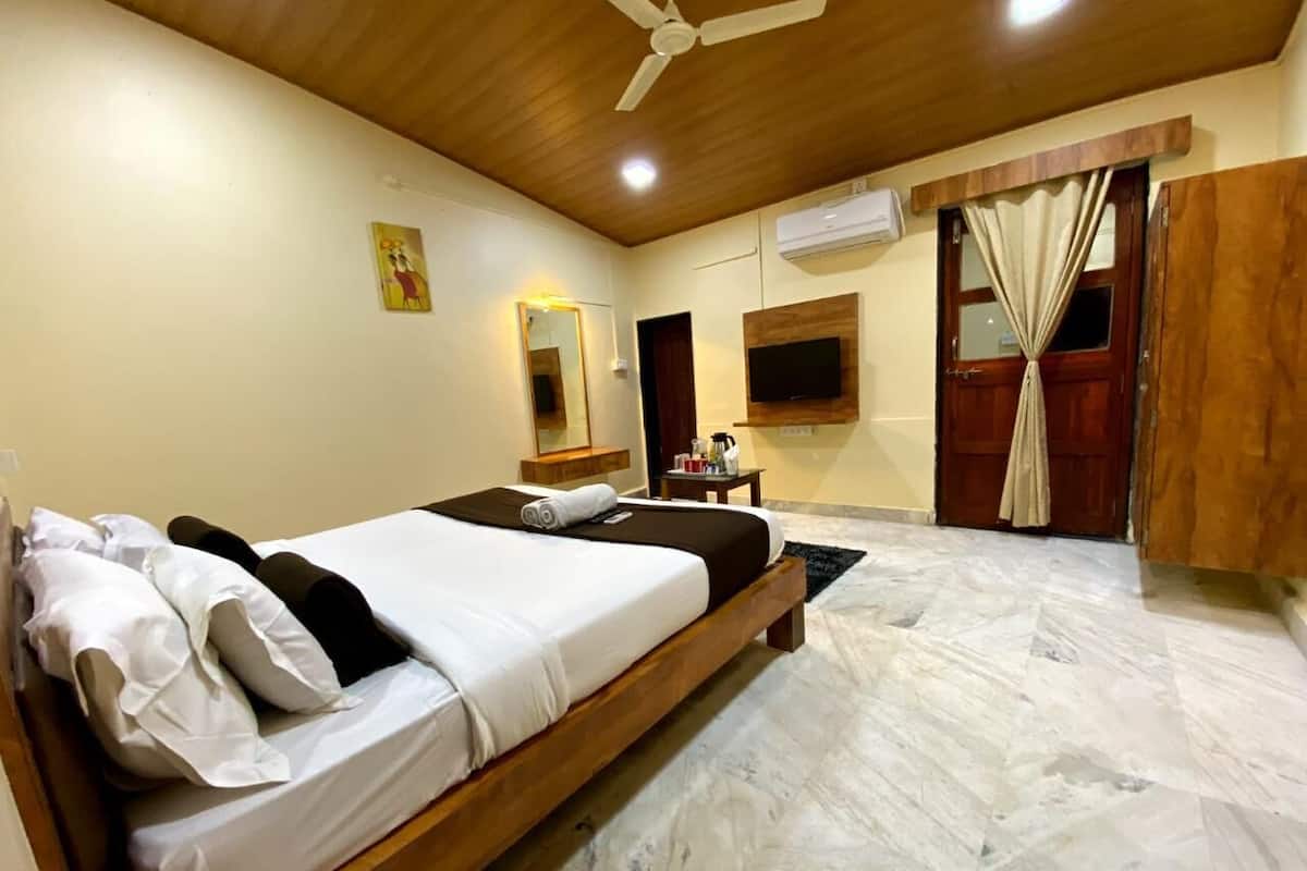 Quarto de hotel com cama grande, ventilador de teto, televisão de tela plana e porta de madeira.