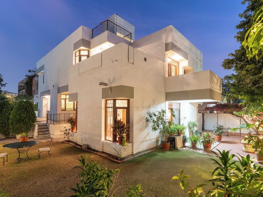 Uma casa moderna de dois andares com telhado plano, janelas amplas e um pátio bem iluminado com plantas em vasos.