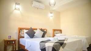 Quarto de hotel com duas camas, uma mesa de cabeceira, ar condicionado fixado na parede e duas arandelas.