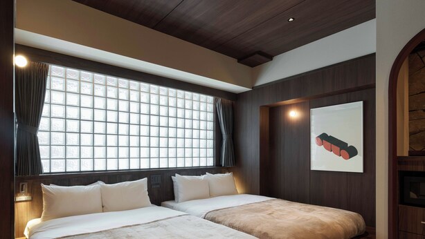 Quarto de hotel com duas camas, uma janela ampla com cortinas, teto de madeira e um quadro na parede.