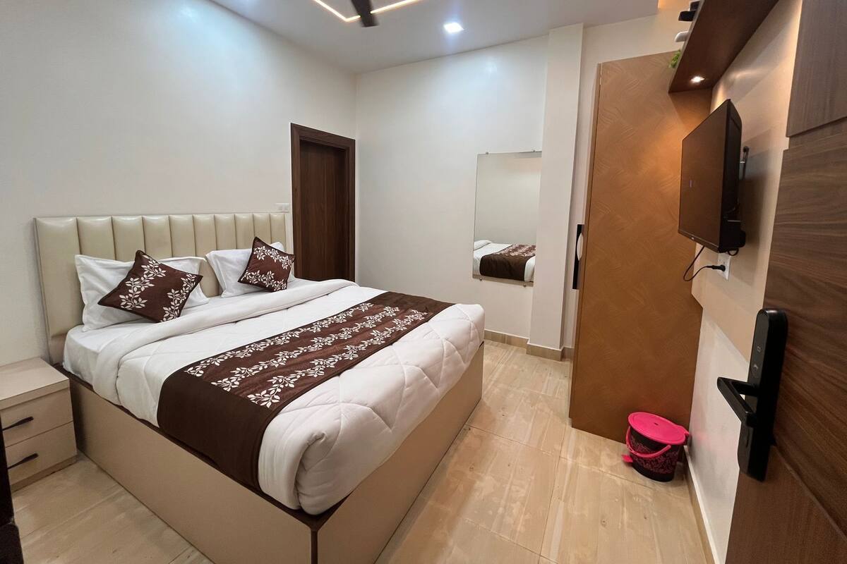 Quarto moderno com cama, mesas de cabeceira, ventilador de teto, TV fixada na parede e porta de madeira.