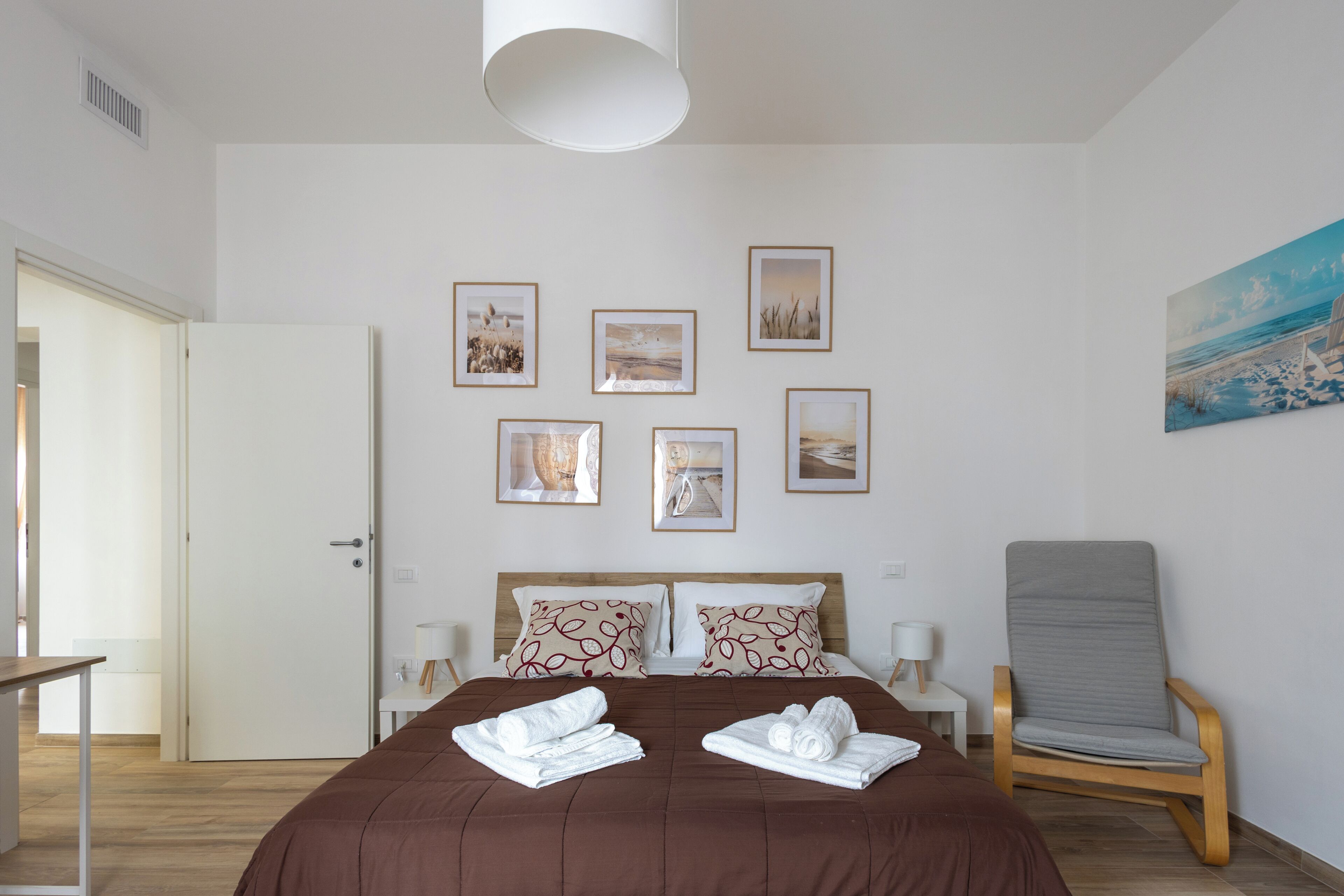 Quarto com cama, almofadas, uma cadeira e quadros na parede.