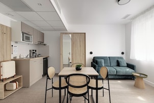 Um apartamento moderno com cozinha compacta, área de refeições com mesa e cadeiras, sofá e uma pequena mesinha lateral.