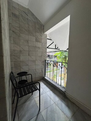 Uma varanda com piso de azulejos, uma cadeira de metal e uma cobertura branca.