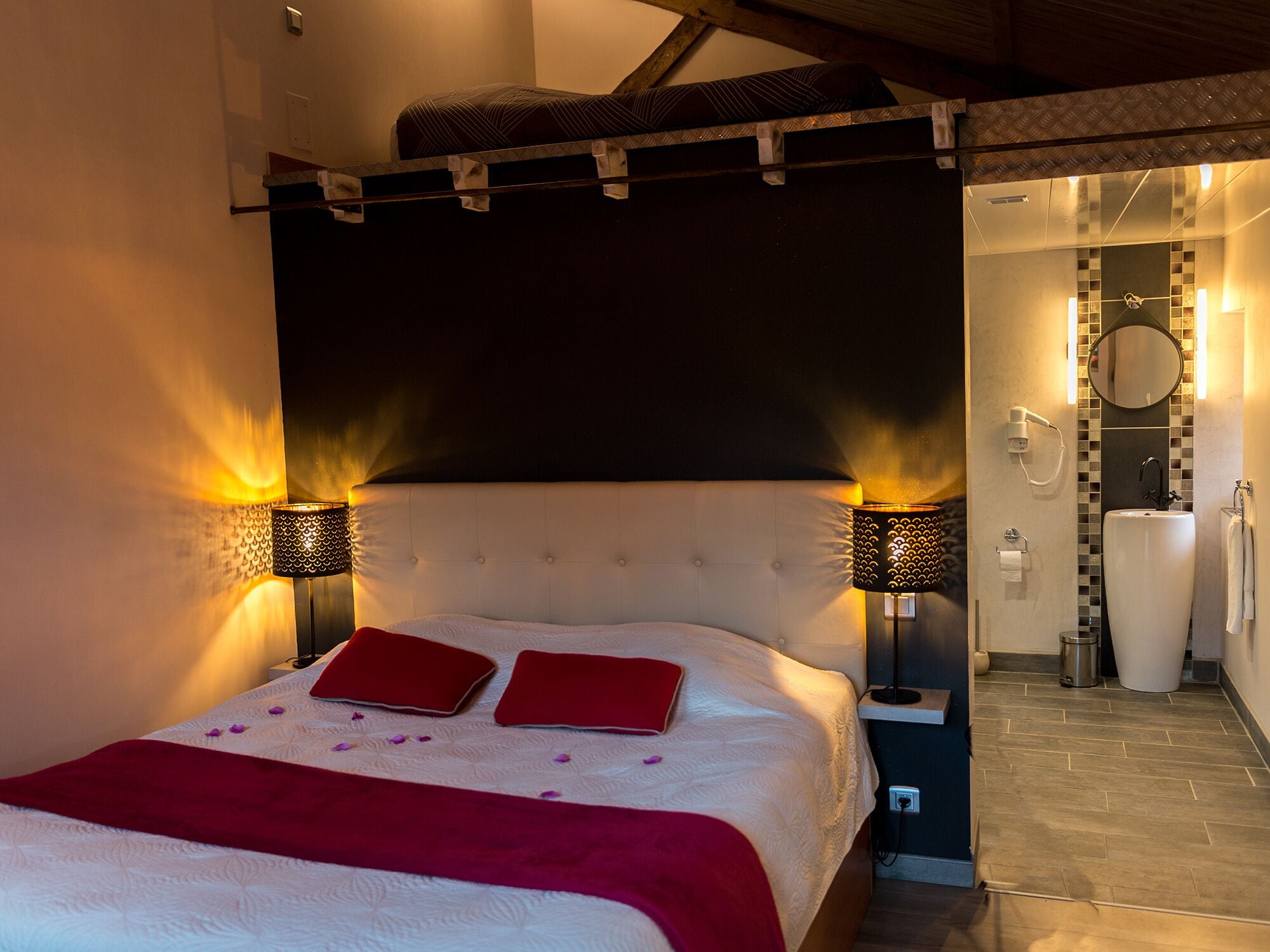 Quarto com cama, duas luminárias de cabeceira, manta vermelha e travesseiro vermelho.