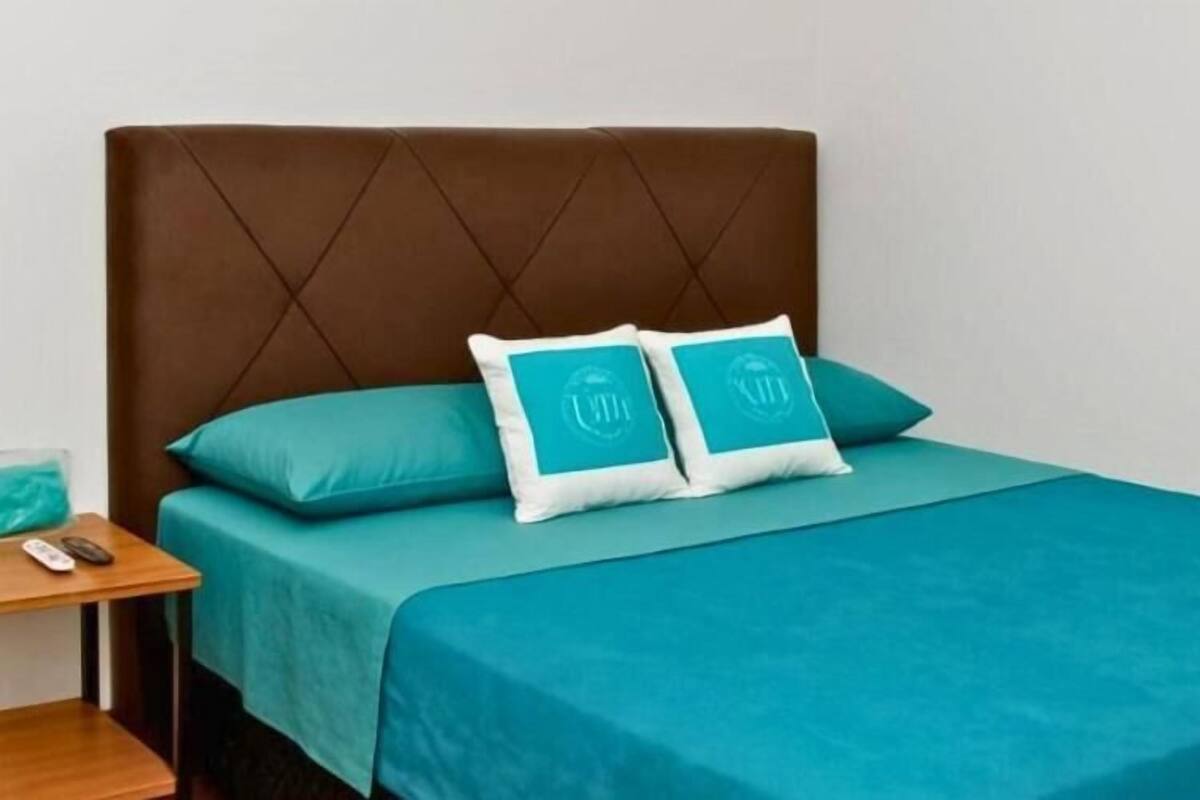 Uma cama com cabeceira marrom, roupa de cama azul-turquesa e dois travesseiros azul-turquesa com detalhes brancos.