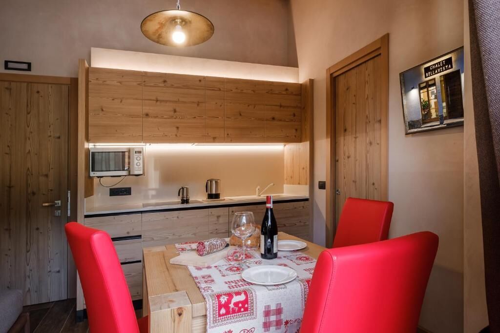 Uma área de refeições com uma mesa de madeira, cadeiras vermelhas, uma garrafa de vinho e uma placa sobre a porta.