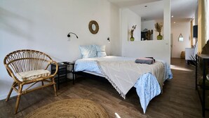 Quarto com uma cama, uma cadeira de vime, uma mesa de cabeceira e um espelho.