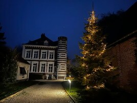 Um edifício grande e histórico com uma torre imponente, um caminho bem iluminado e um pinheiro de Natal decorado.