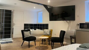 Quarto de hotel moderno com uma cama grande, duas cadeiras pretas, uma mesa redonda pequena, uma banheira, uma televisão e um micro-ondas.