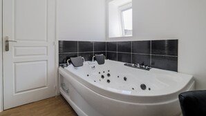 Um banheiro moderno com uma banheira grande, paredes revestidas de azulejos pretos, uma janela e uma porta branca.