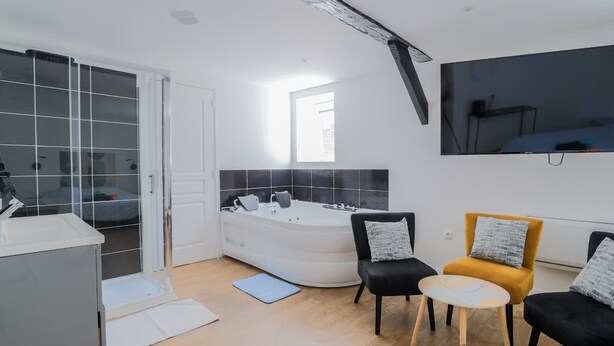 Quarto moderno com uma banheira grande, duas cadeiras, uma mesa pequena e televisão na parede.