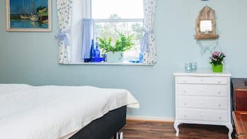 Quarto com cama, penteadeira, janela com cortinas, relógio, quadro e planta em vaso.