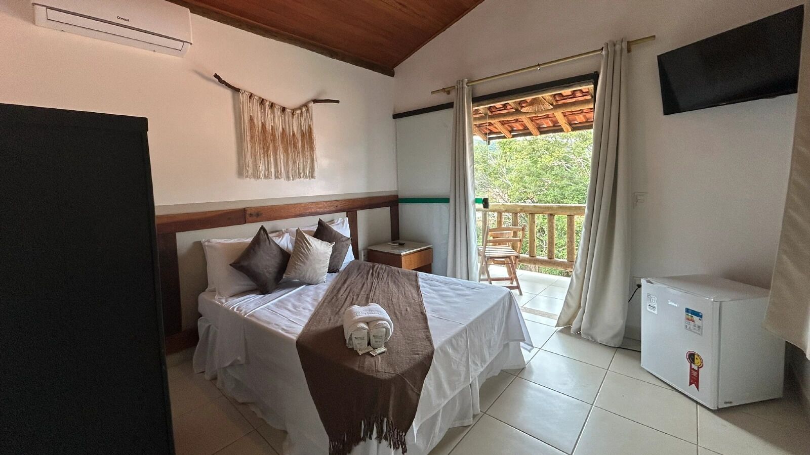 Quarto de hotel com cama, uma mesinha, televisão e varanda com vista.