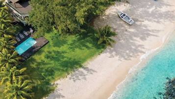 Vista aérea de uma praia com piscina, barco e vegetação exuberante.