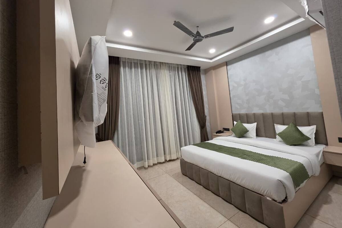Quarto de hotel com cama, ventoinha no teto, mesa de cabeceira e janela com cortinas.
