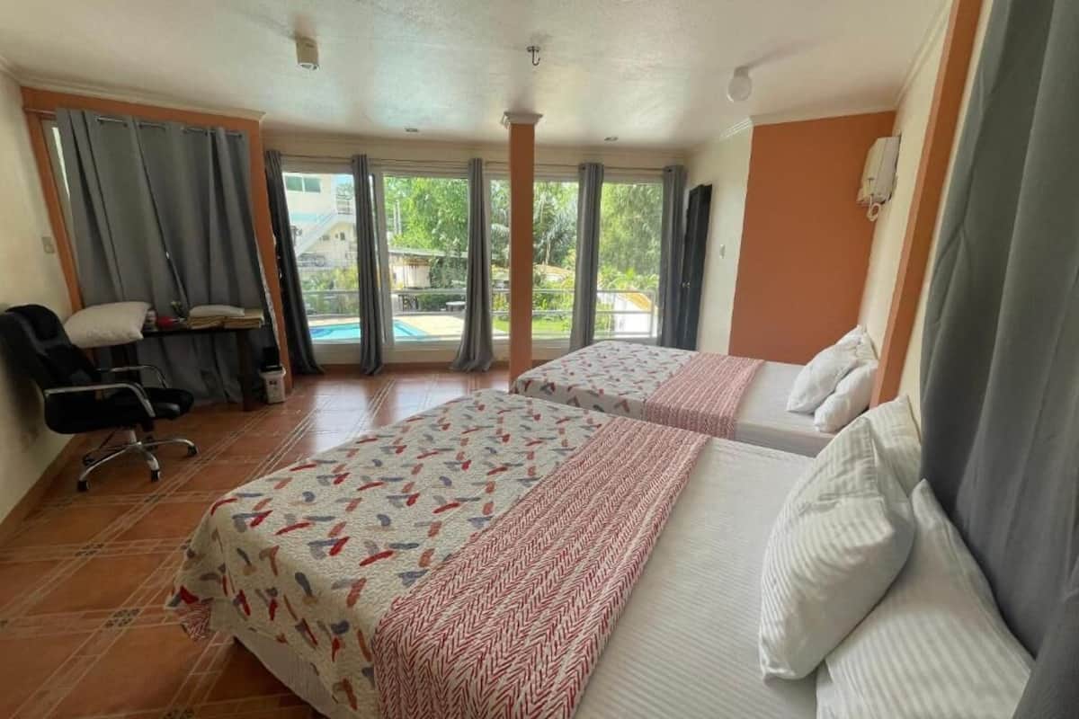 Quarto de hotel com duas camas, uma escrivaninha, uma cadeira e vista para uma piscina.