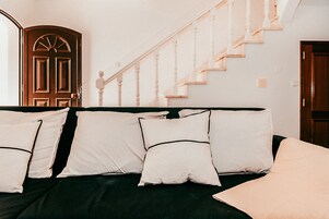 Uma cama com travesseiros brancos, um edredom verde escuro e uma escada de madeira ao fundo.