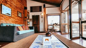 Quarto com parede de madeira, um sofá, uma mesa com o logotipo GT HOUSE e vista através de uma porta de vidro.