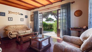 Sala de estar com sofá, mesa de centro e vista para um jardim através de uma porta de vidro.