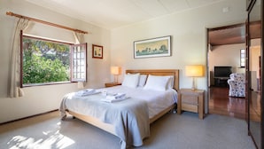 Quarto de hotel com cama, luminárias de cabeceira, um quadro, janela com cortinas e vista para o verde lá fora.