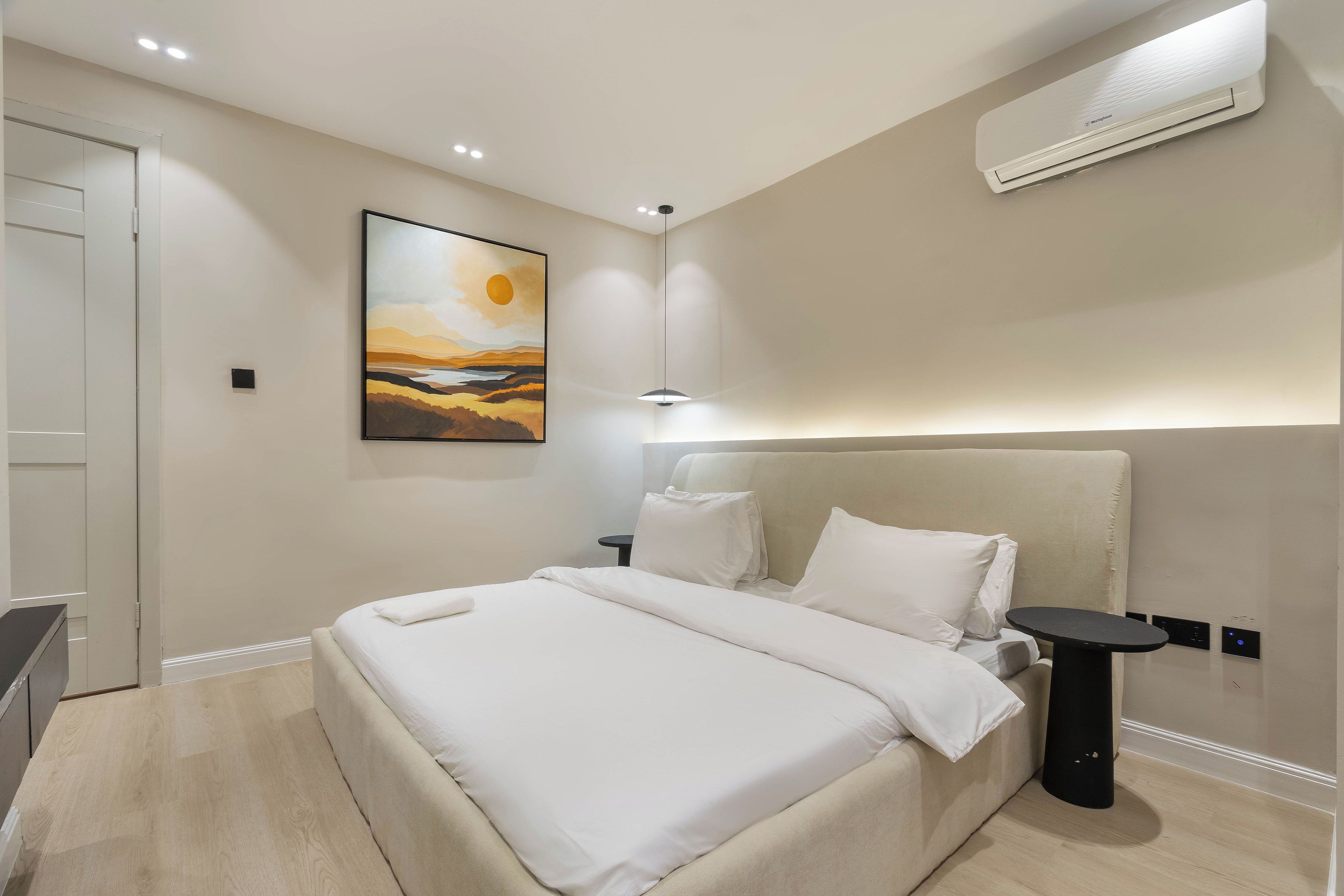 Quarto com cama, mesa de cabeceira, ar condicionado fixado na parede e um quadro.