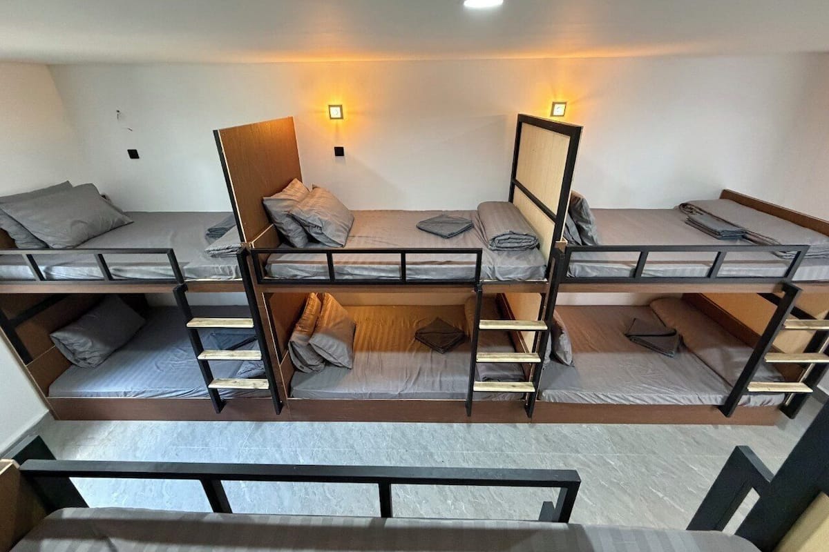 Quarto com beliche, duas camas, escada de madeira e luminárias fixadas na parede.