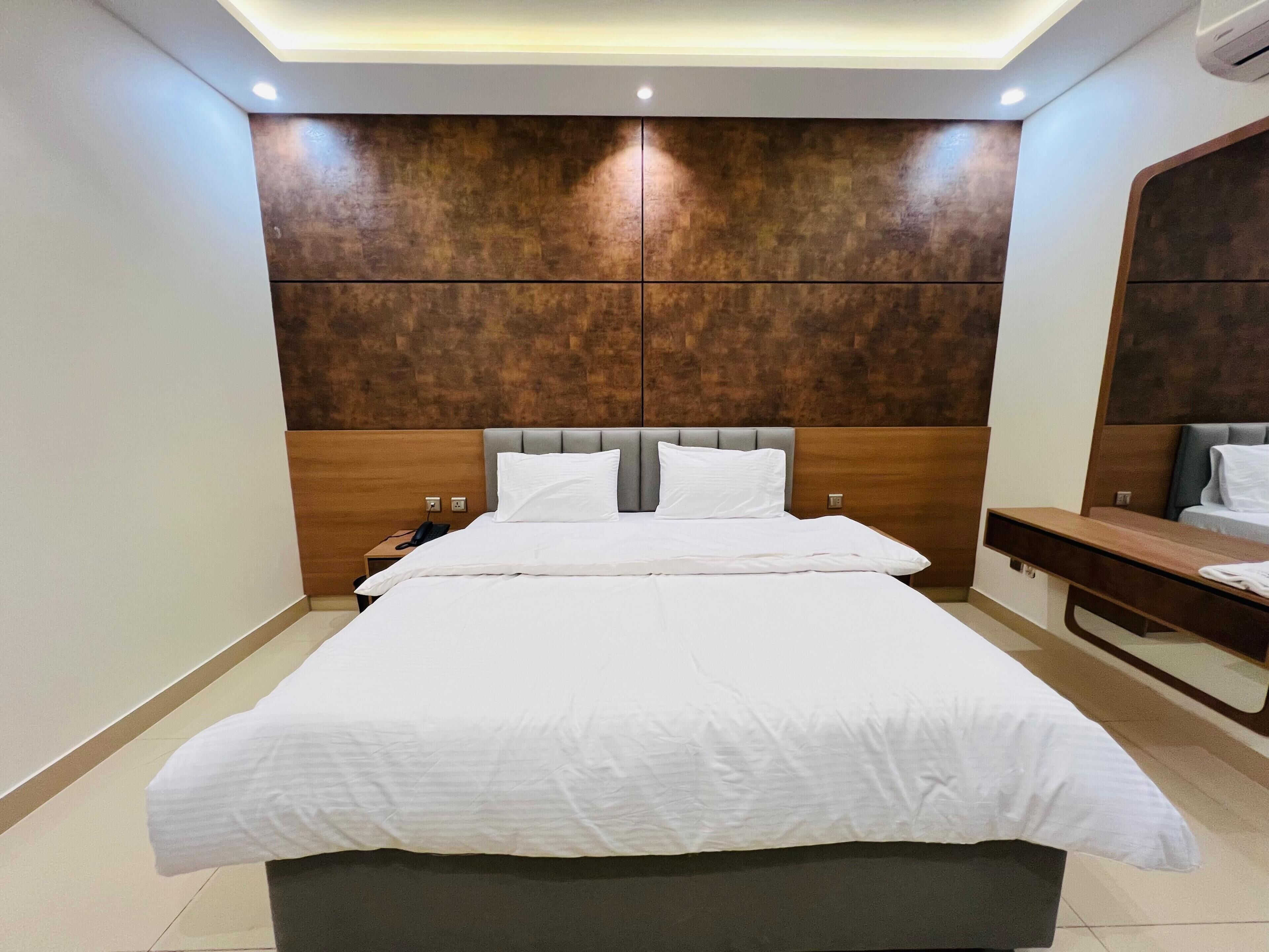 Quarto de hotel moderno com uma cama grande, mesa de cabeceira e um banco embutido.