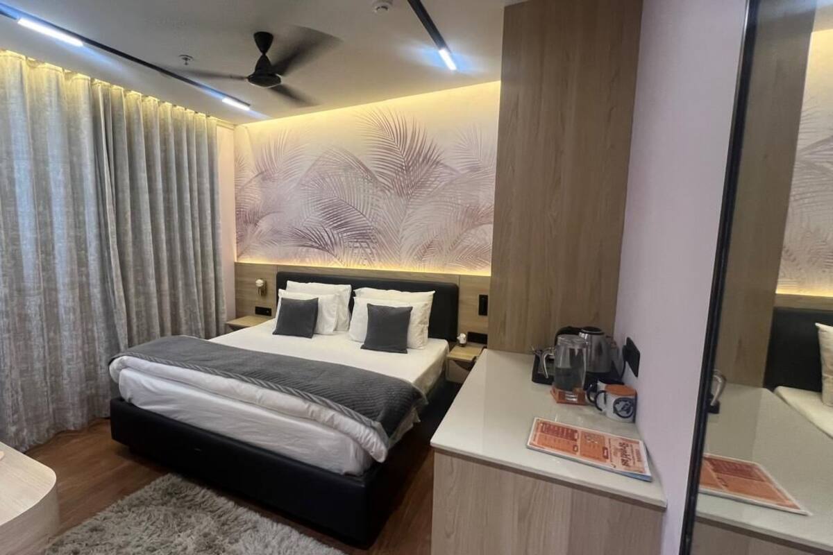 Quarto de hotel moderno com cama, mesa de cabeceira e um espelho grande.
