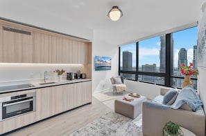 Uma cozinha moderna com eletrodomésticos embutidos, uma sala de jantar com sofá e mesa de centro, e uma grande janela com vista para a cidade.