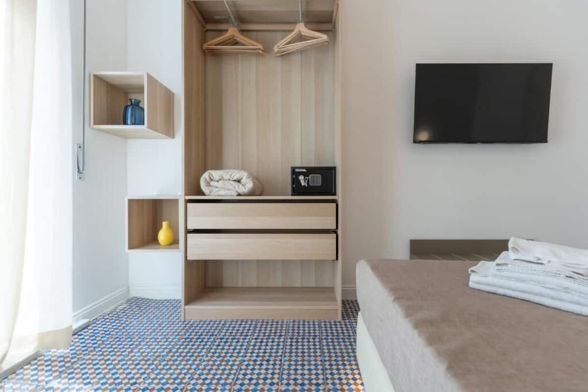 Quarto com cama, televisão, guarda-roupa e uma pequena estante com um vaso.