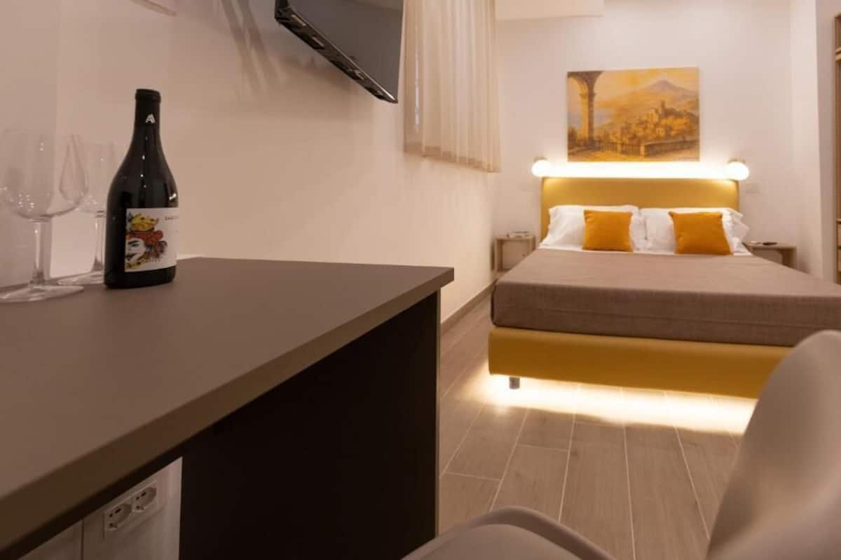 Quarto de hotel com cama, mesa de cabeceira e uma garrafa de vinho.