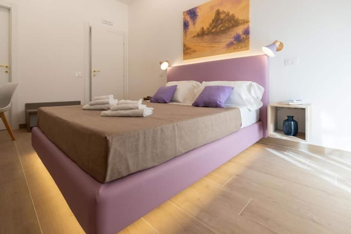 Quarto com uma cama, mesa de cabeceira, cadeira e um quadro na parede.