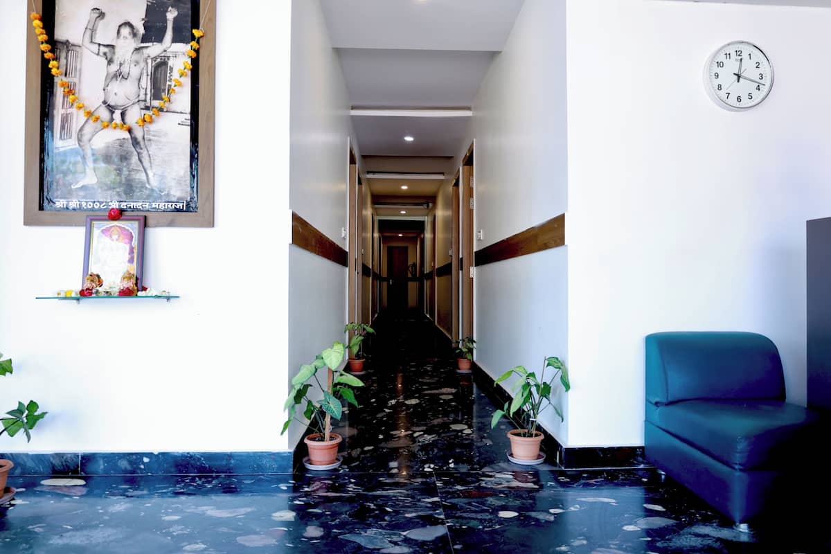 Um hall de hotel com piso de mármore, uma poltrona azul, um relógio e uma moldura com um quadro na parede.