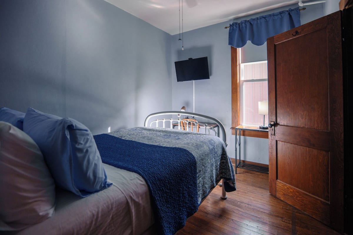 Quarto com cama, porta de madeira, janela com vista e televisão de tela plana na parede.