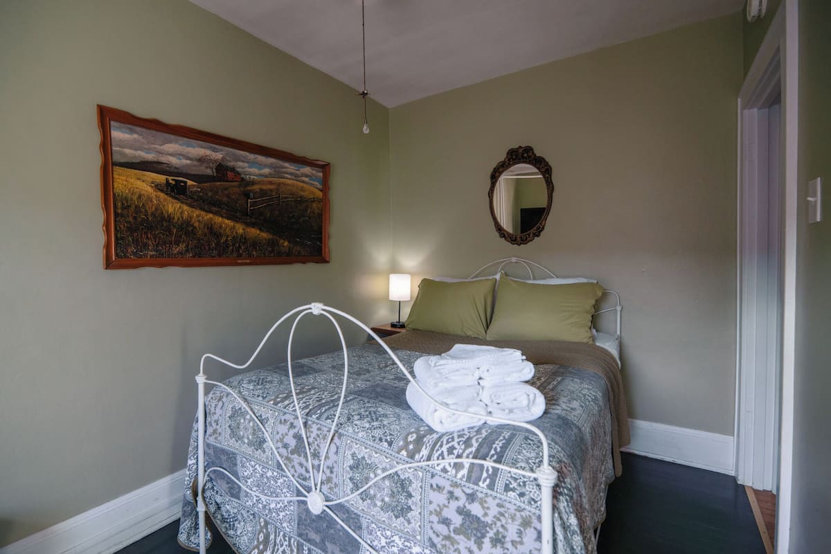 Um quarto com cama, quadro, espelho e luminária de cabeceira.