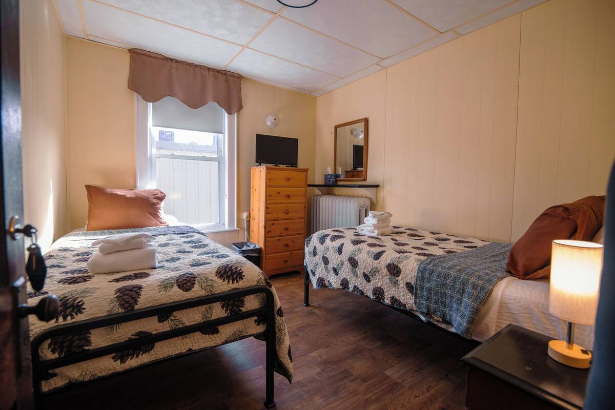 Quarto com duas camas, cómoda, espelho e abajur.