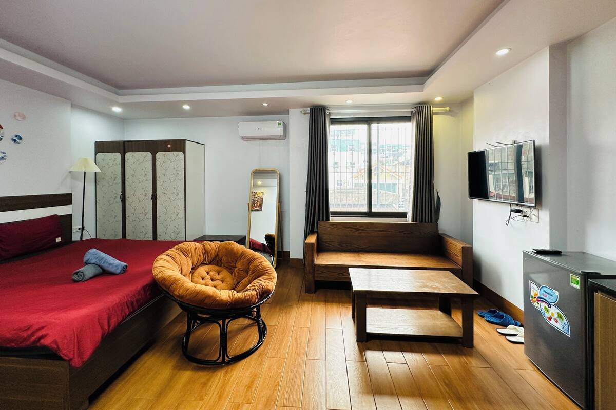 Quarto com cama, poltrona, sofá, televisão, guarda-roupa e janela.