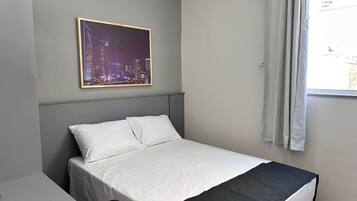 Um quarto com uma cama, uma cadeira, uma janela com cortinas e um quadro com uma vista da cidade.