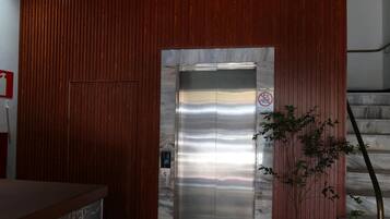 Um elevador com acabamento em aço inoxidável, um aviso de proibido fumar e uma parede revestida de madeira.