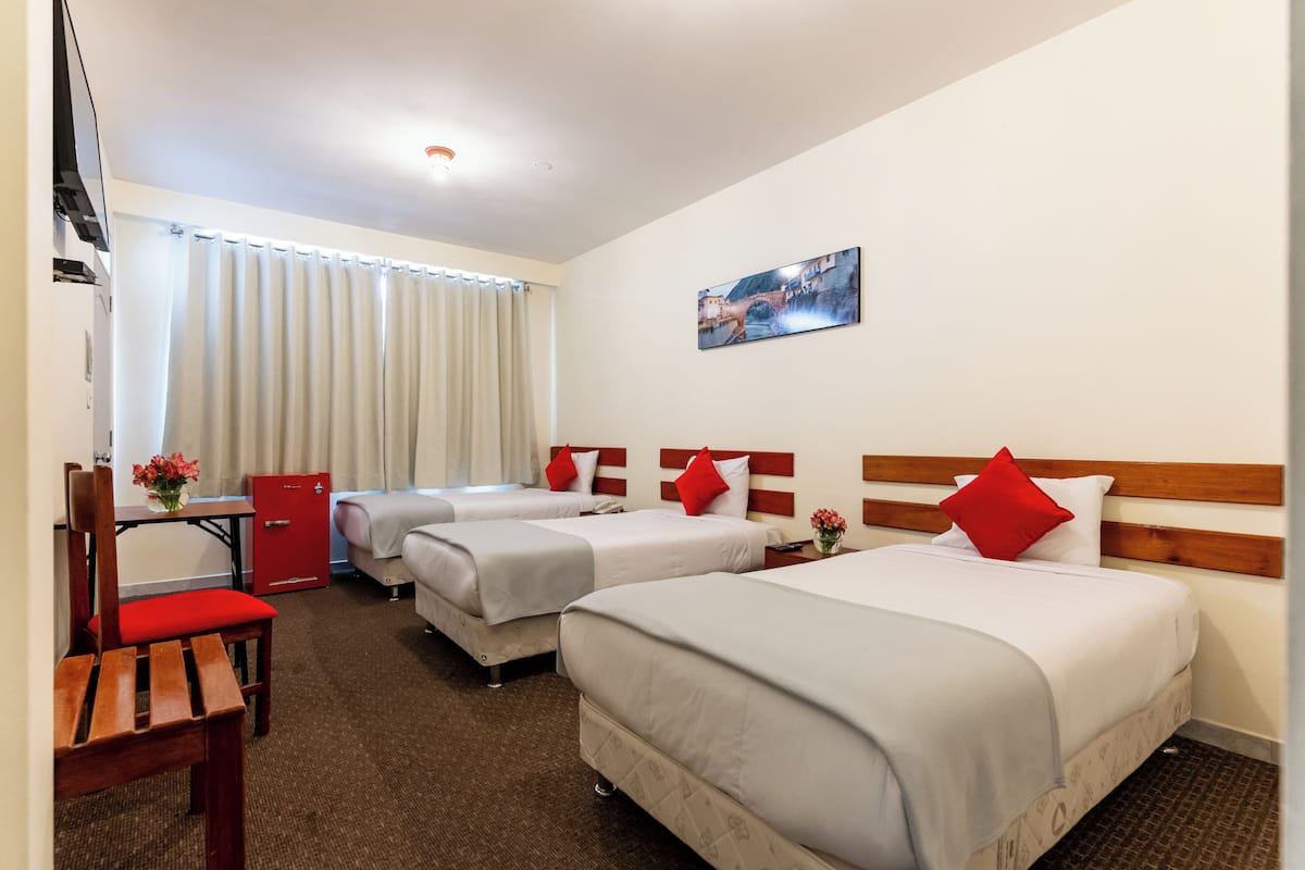Quarto de hotel com duas camas, uma escrivaninha, uma cadeira, um armário vermelho e uma pintura na parede.