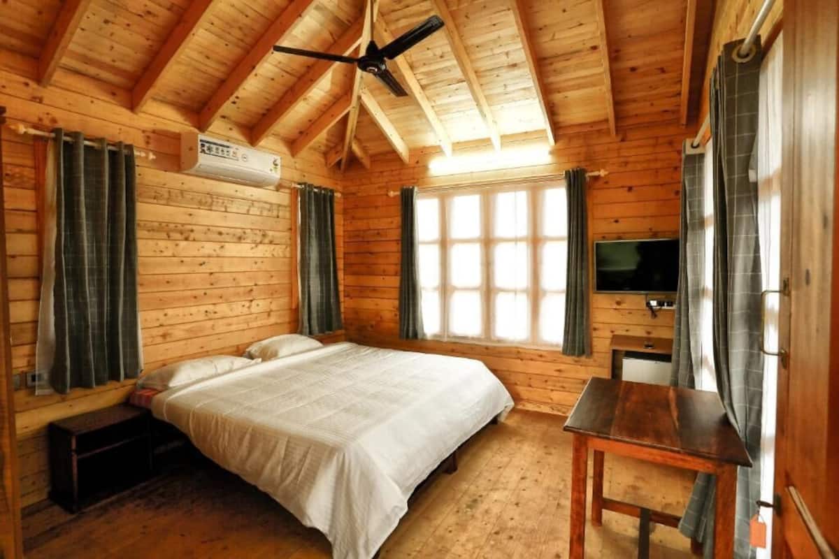 Quarto de cabana de madeira com uma cama, escrivaninha, televisão e ventoinha no teto.