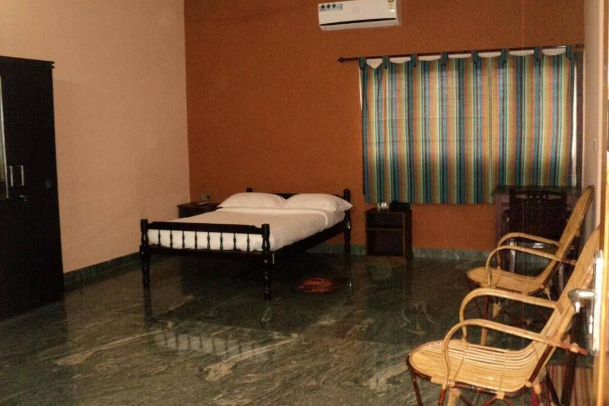 Quarto com cama, mesa de cabeceira, cadeira, guarda-roupa e janela com cortinas.