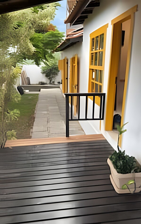 Um deck de madeira com guarda-corpo, um vaso de planta e um caminho que leva a um edifício com portas amarelas.