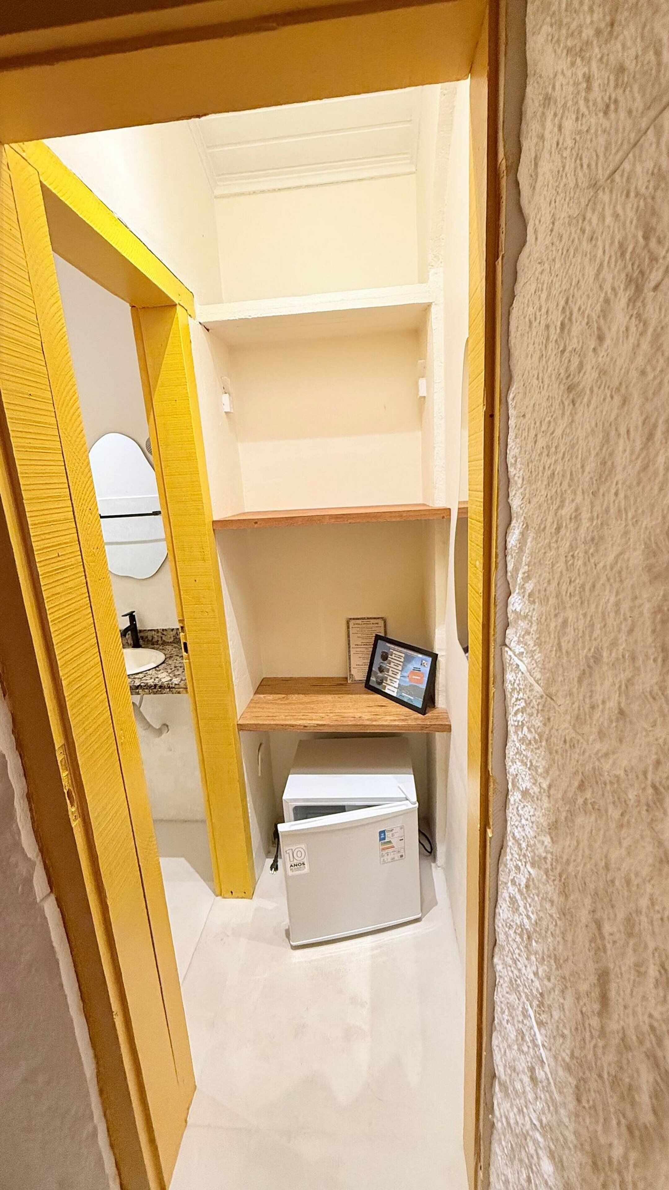 Quarto compacto com um banco embutido, um pequeno frigorífico e um quadro emoldurado sobre o banco.
