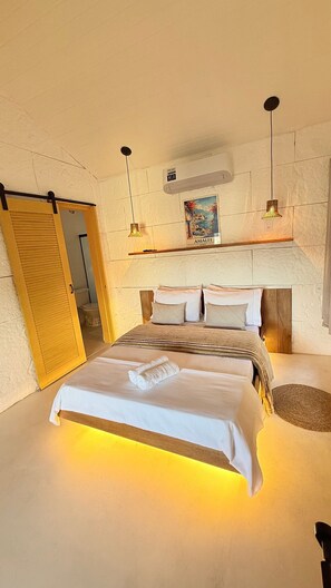 Quarto com cama, luminárias de cabeceira, um quadro e uma porta que dá para outro espaço.