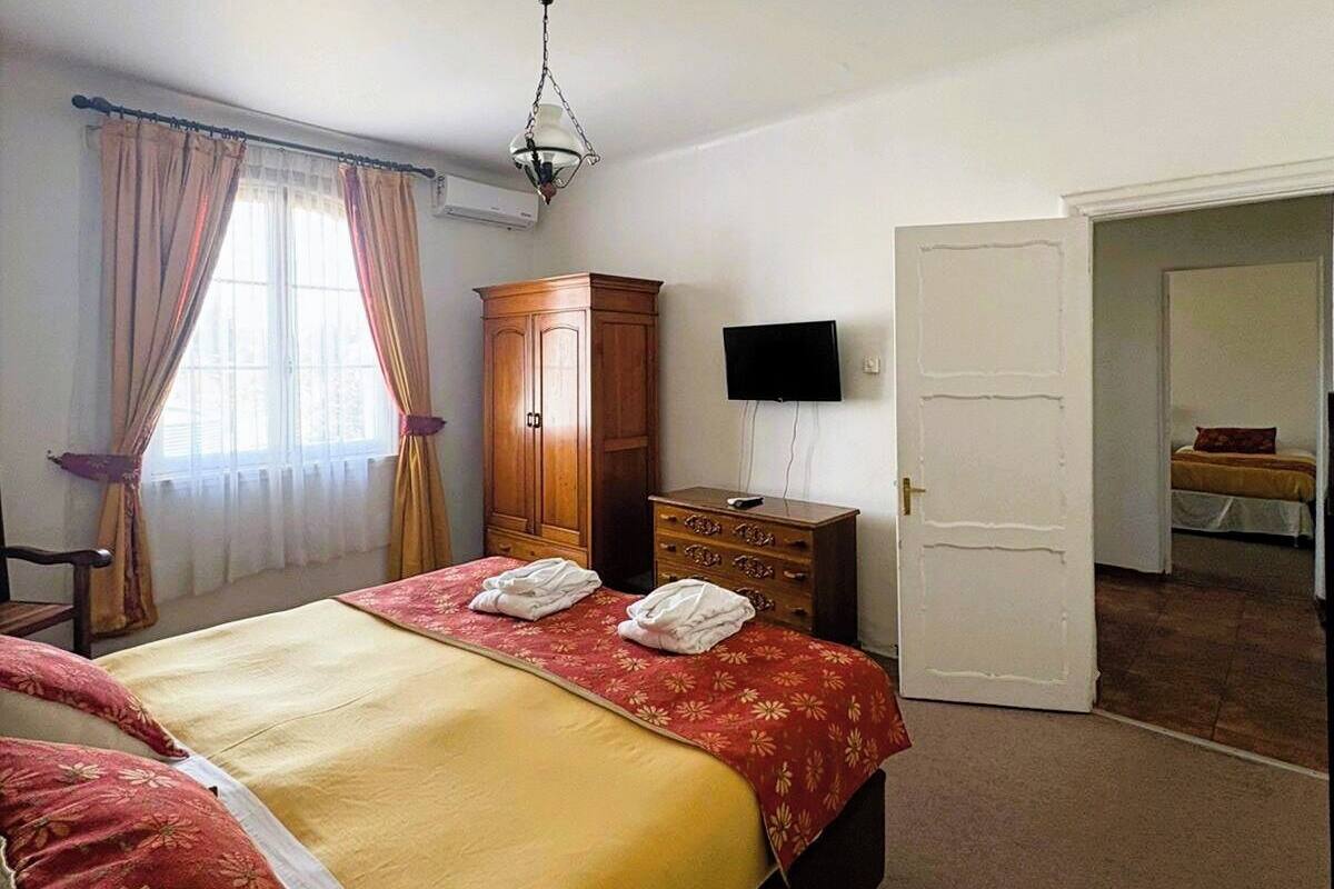 Quarto de hotel com uma cama, um guarda-roupa, uma televisão e uma porta que dá para outro cômodo.