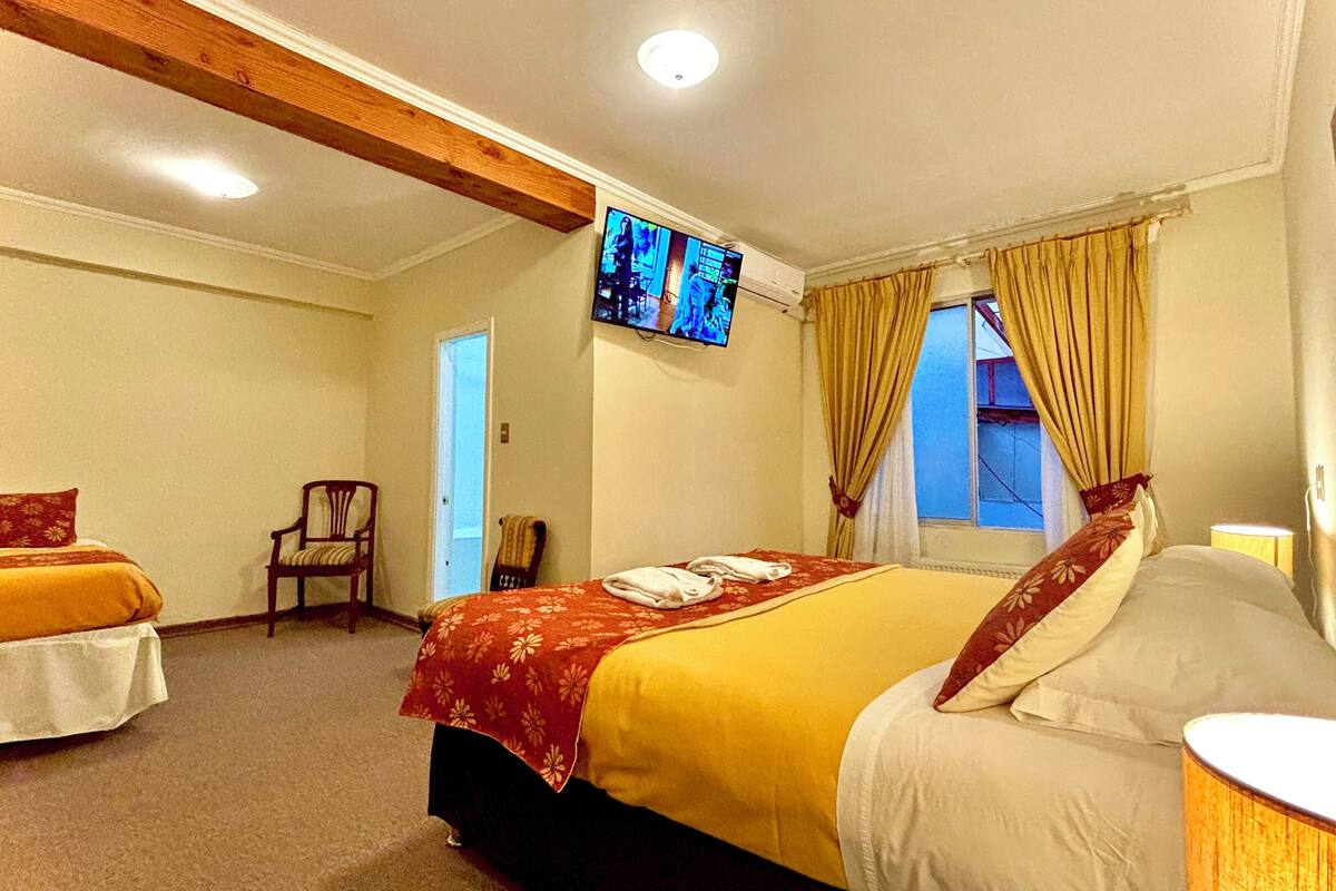Quarto de hotel com duas camas, televisão, uma cadeira e janela com cortinas.